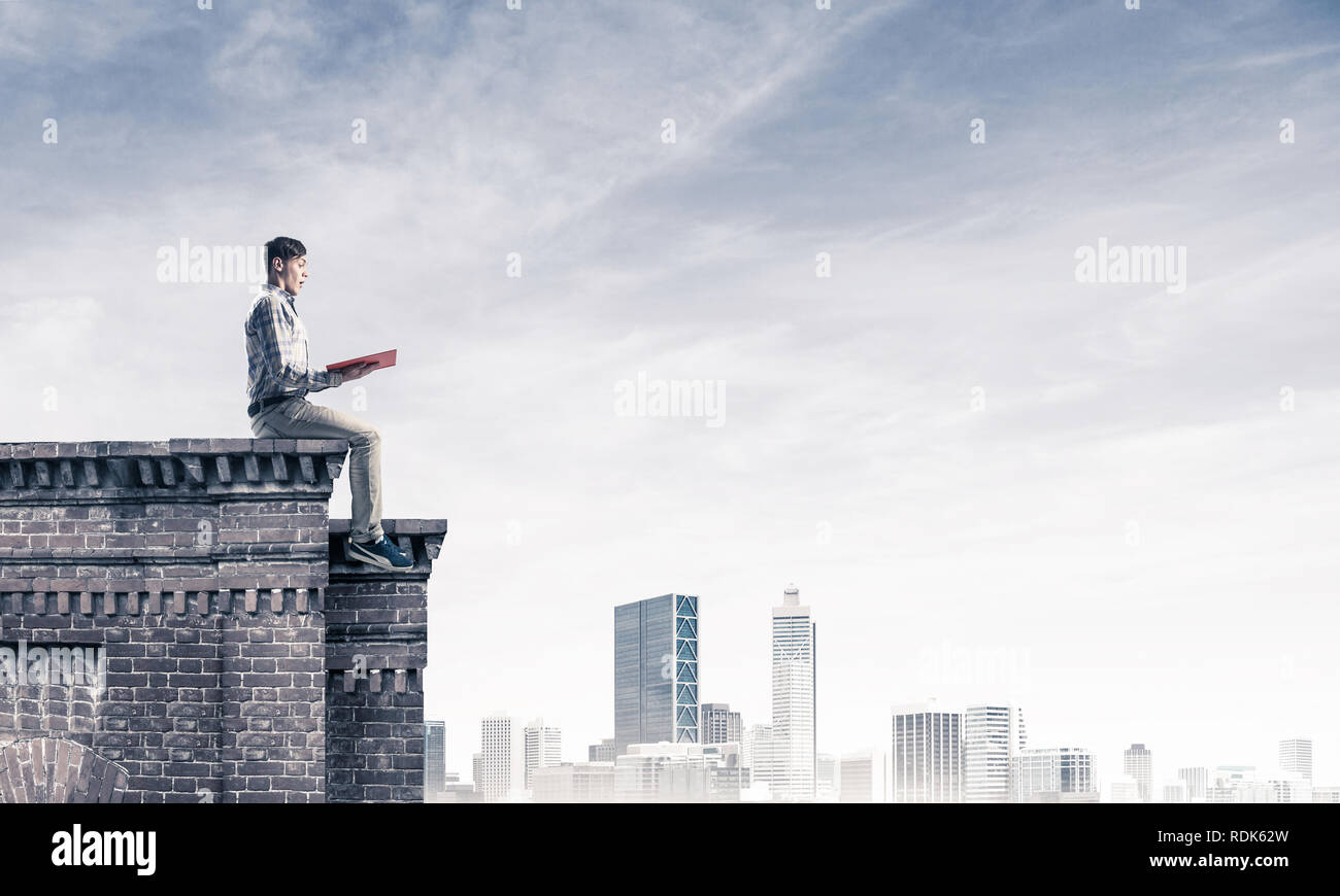 Man on roof edge reading book and cityscape at background Stock Photo ...