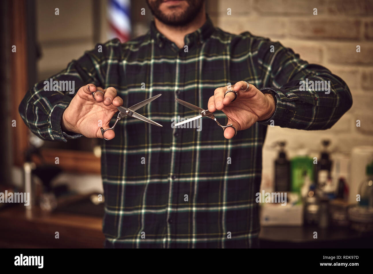 Man hairdresser in a plaid shirt holding a sharp professional scissors ...