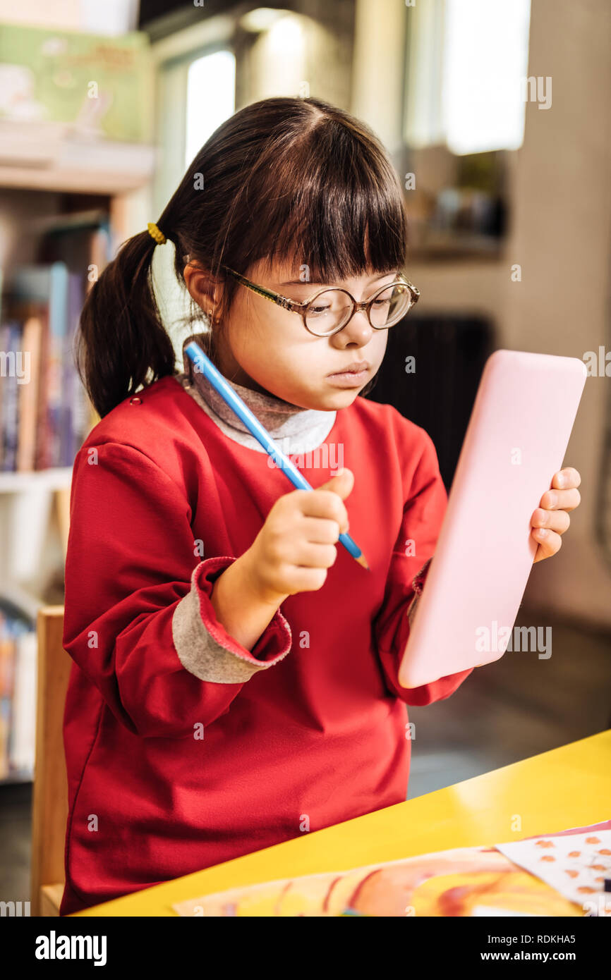 Dark-haired girl with genetic disorder holding blue pencil while ...