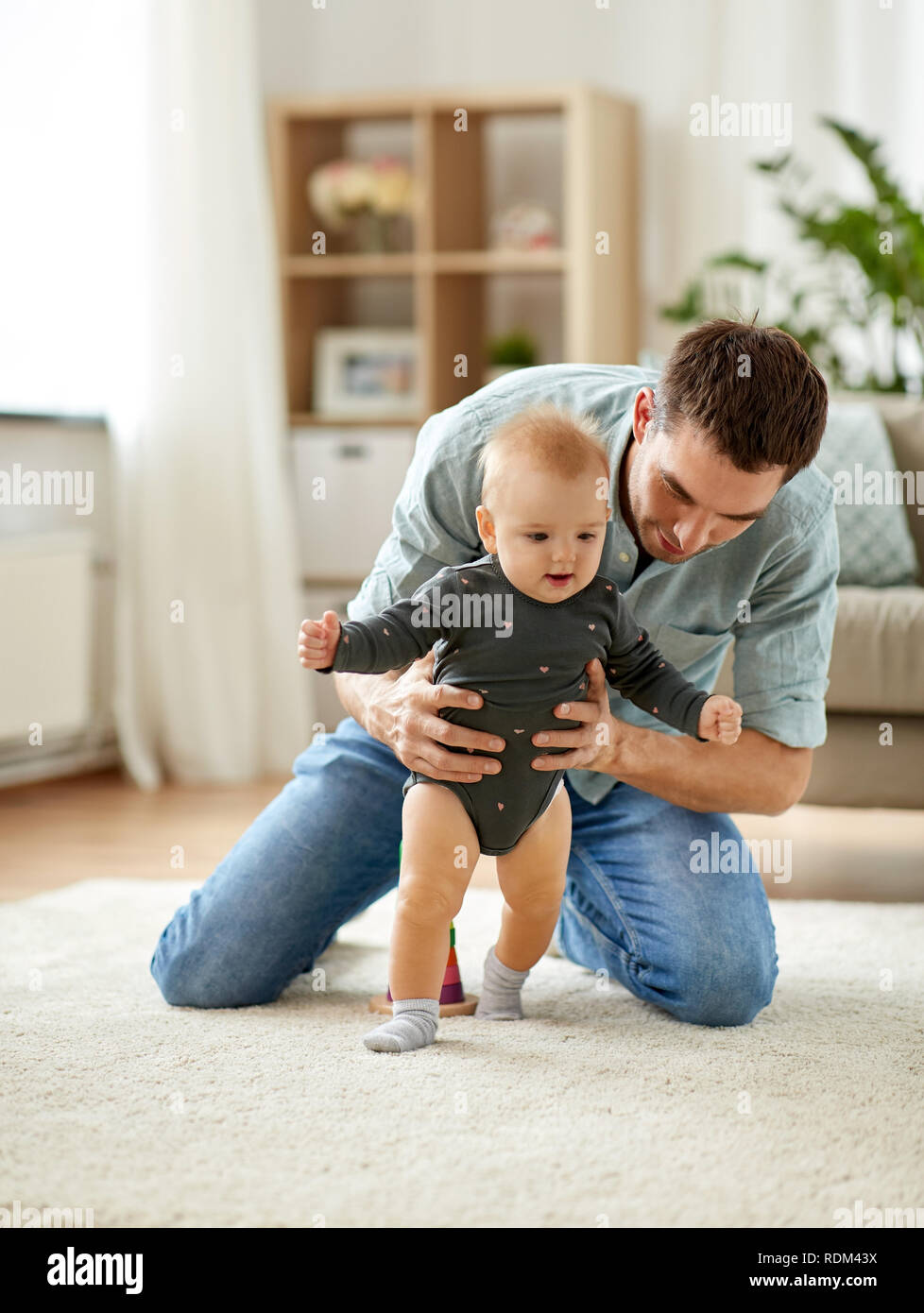 father helping baby daughter with walking at home Stock Photo - Alamy