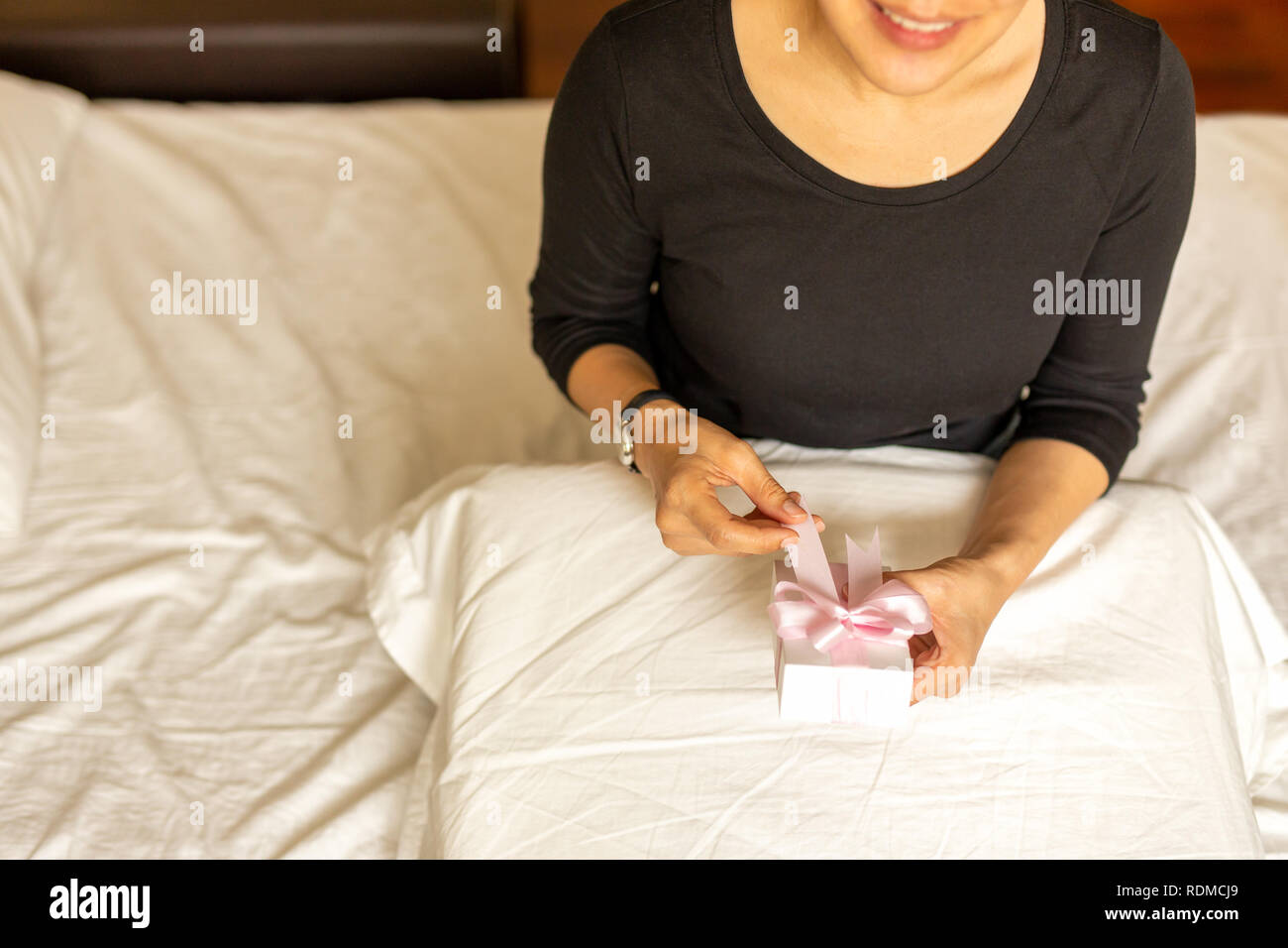 Woman smiling with hands opening valentine presents in bedroom Stock ...