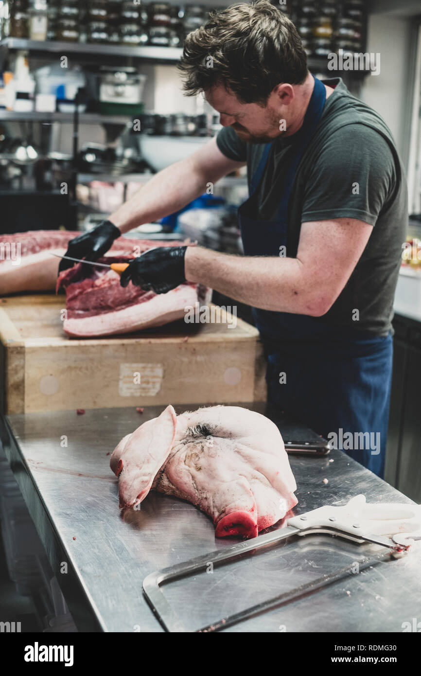Male butcher wearing apron and black rubber gloves cutting pork ribs on ...