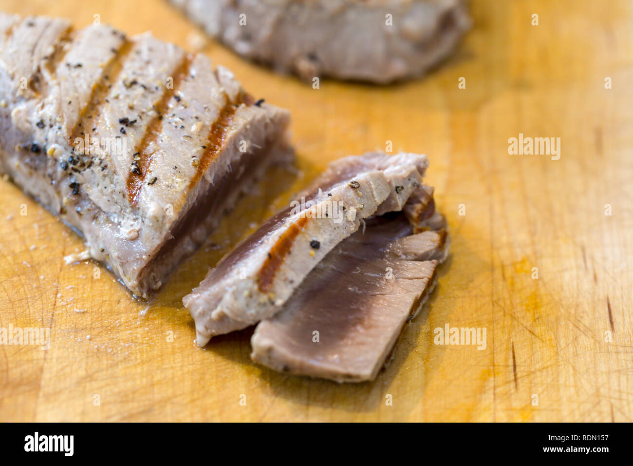 Chargrilled, seasoned tuna steaks cooked and sliced on a wooden ...