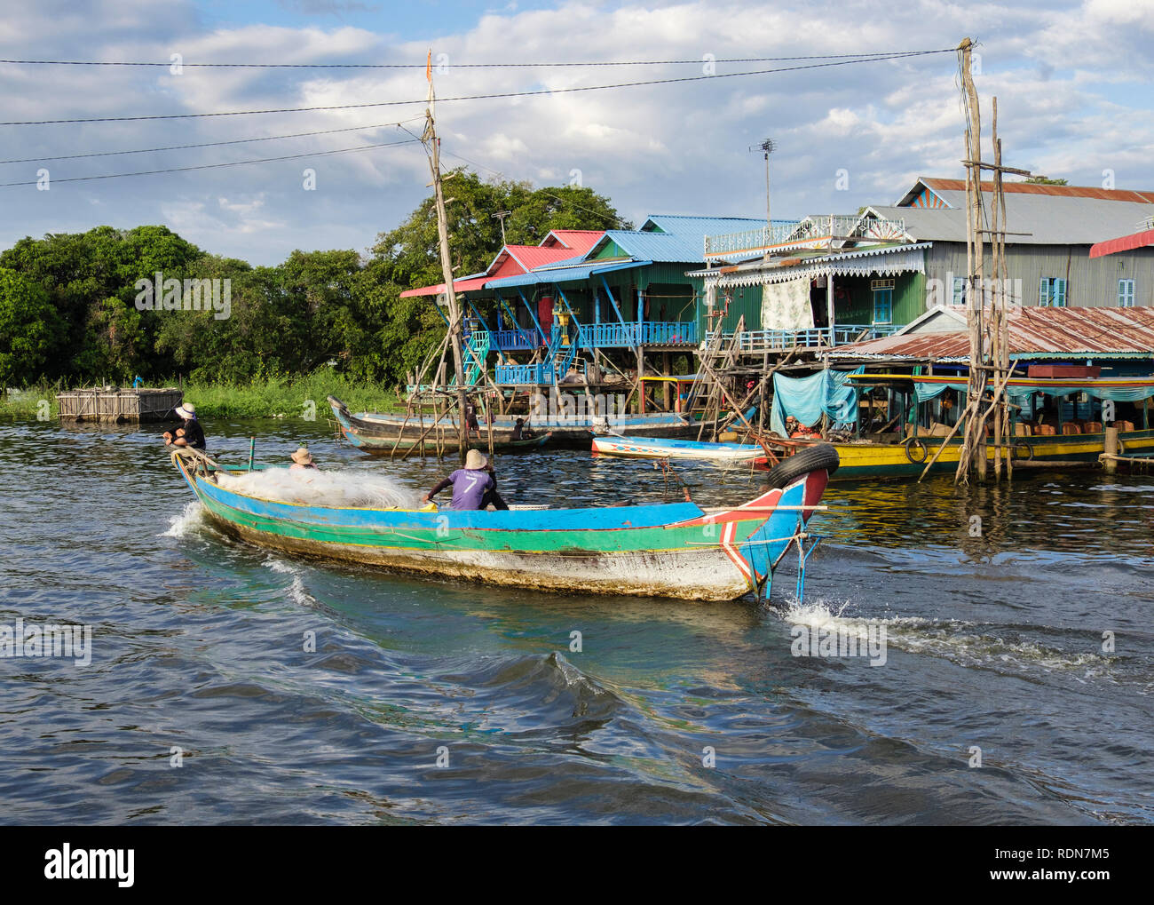 Local fishermen in a fishing boat passing houses on stilts in floating ...