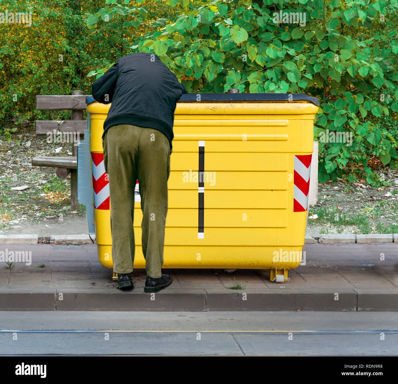 Man digging through garbage in yellow recycling container on the street ...