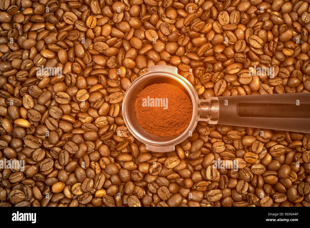 Metal espresso machine scoop with ground coffee on roasted coffee beans ...