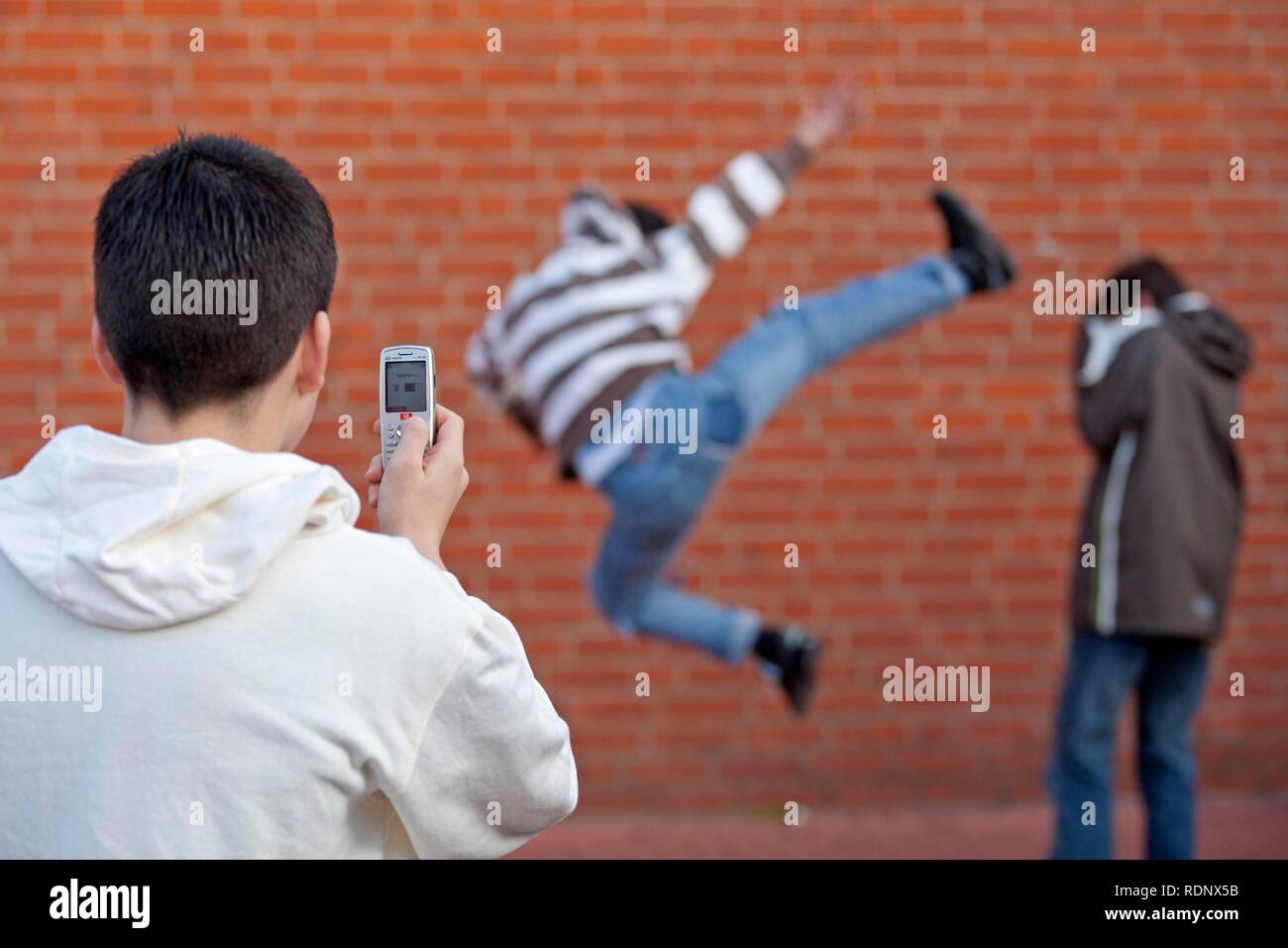 Boy attacking another boy with a karate kick while a third films with ...
