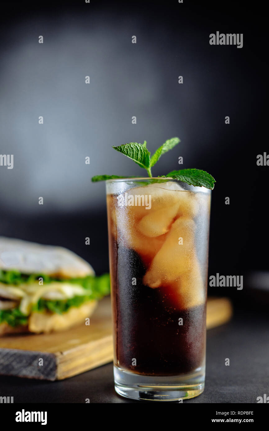 Glass of cola with ice and mint on black background big sandwich ...