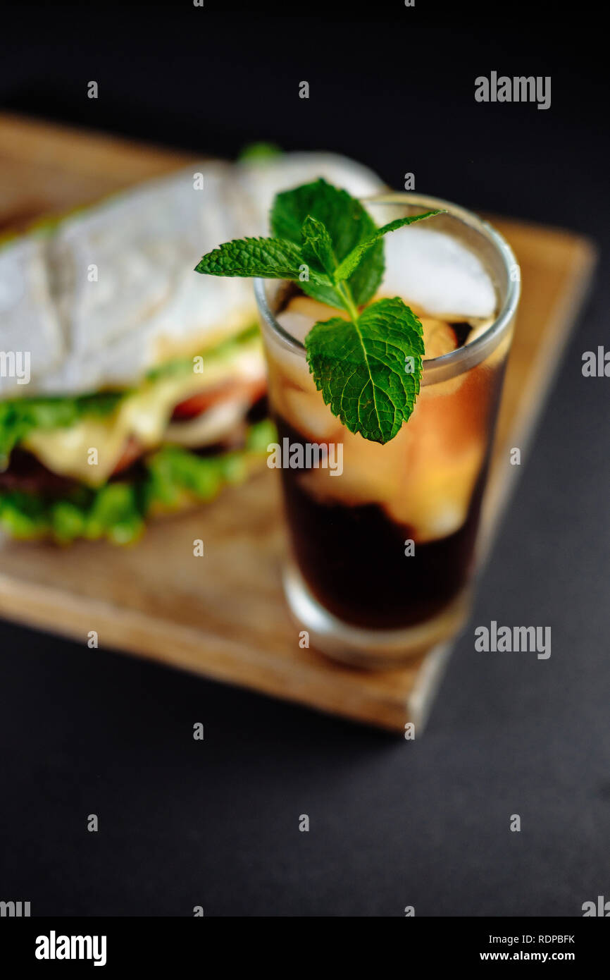 Glass of cola with ice and mint on black background big sandwich ...