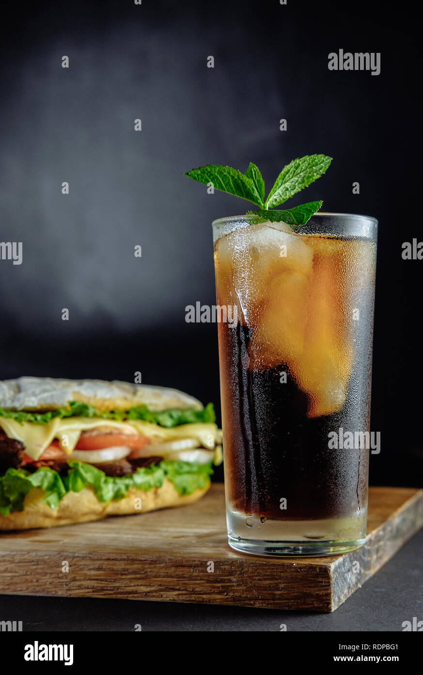 Glass of cola with ice and mint on black background big sandwich ...