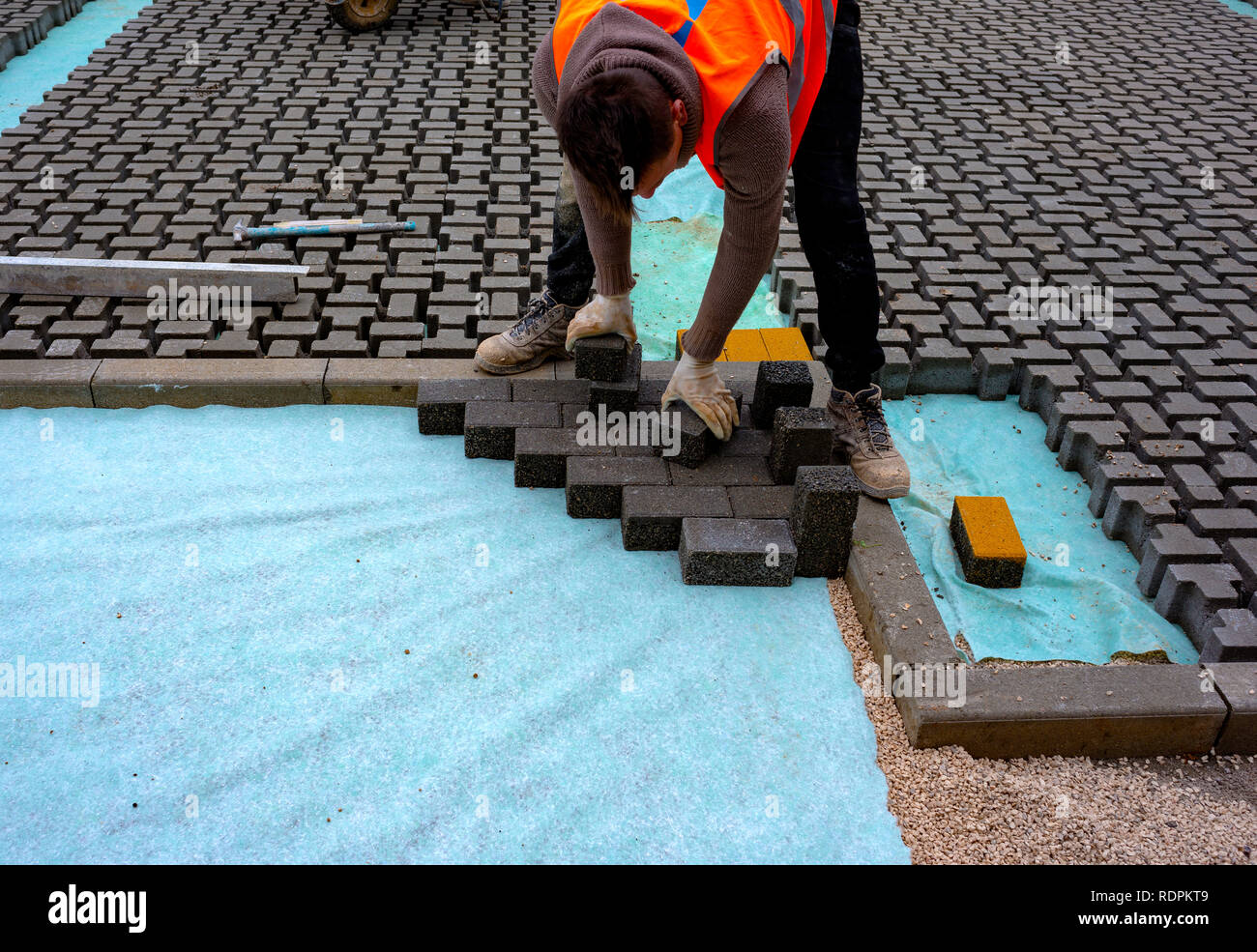 Construction worker laying interlocking paving concrete onto sheet ...