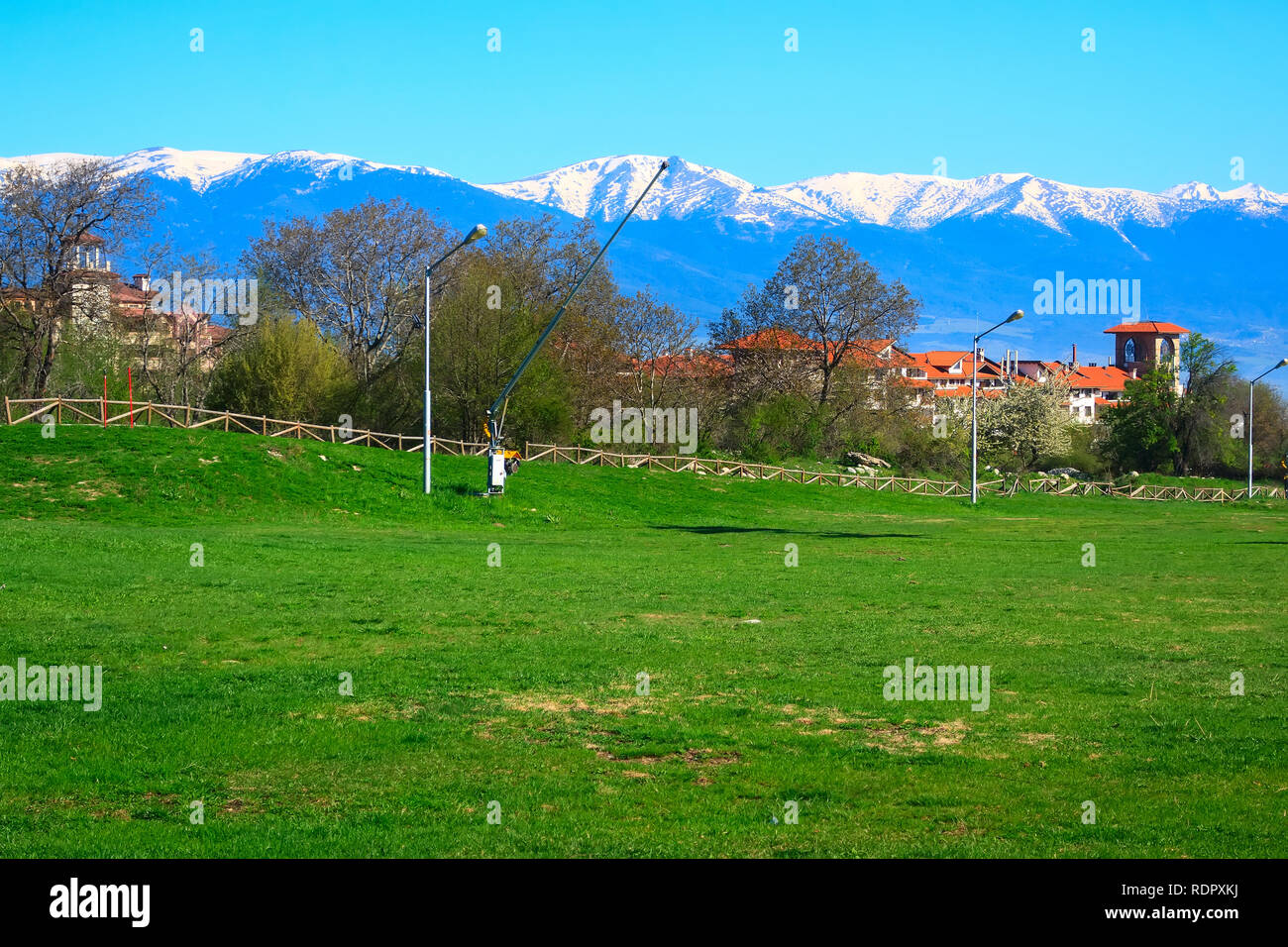Spring landscape with green grass, houses roofs and snow mountain peaks ...