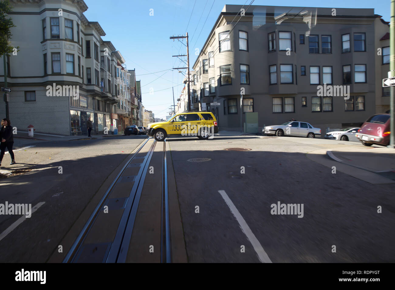 A yellow taxi drives across The world famous San Francisco Cable car ...