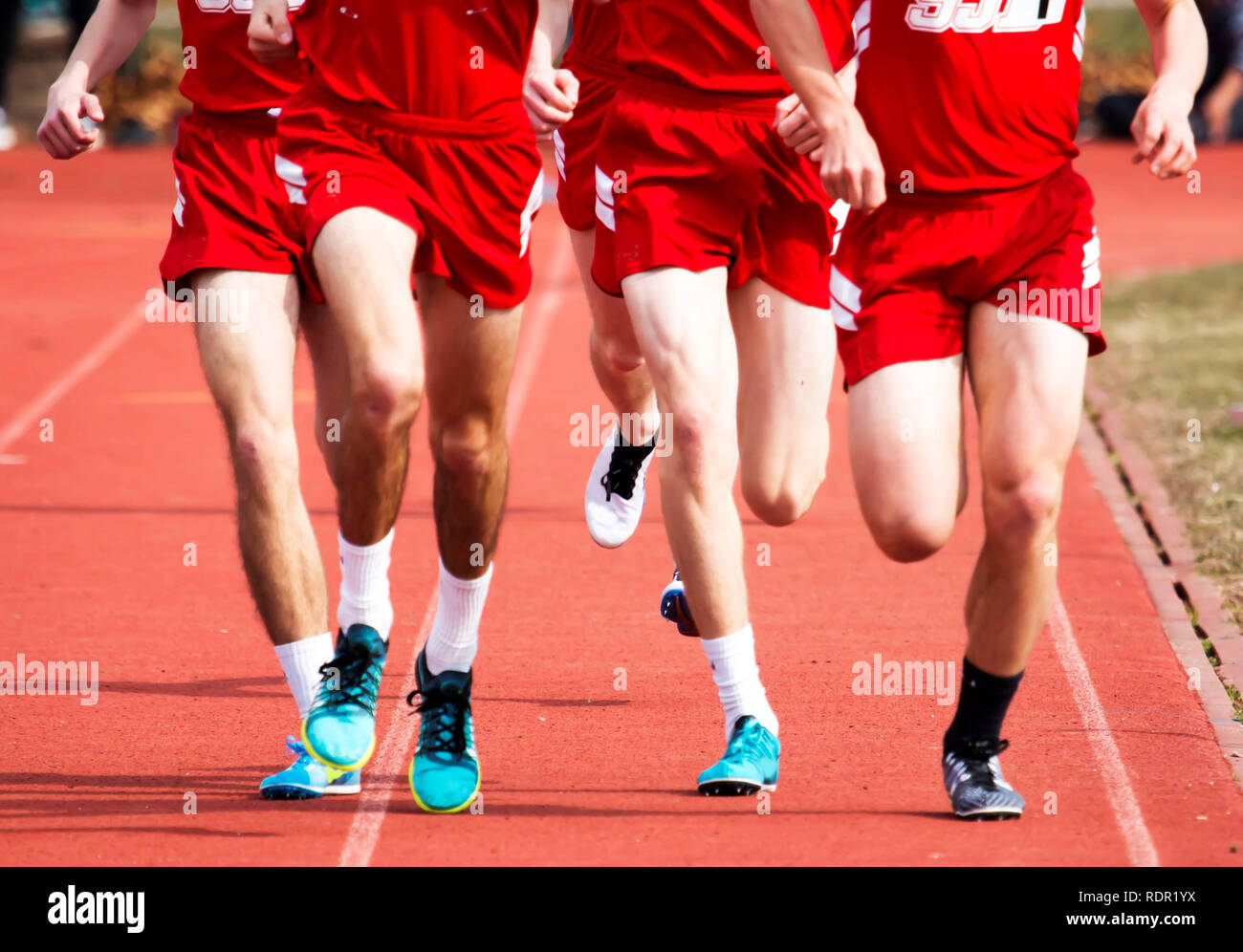 Boys from one team dominate the mile racing on a red track, wearing red ...
