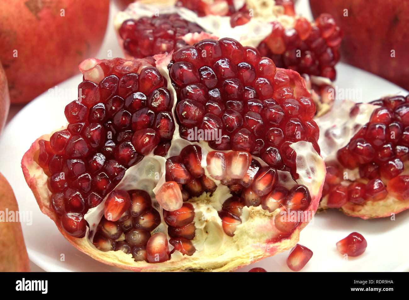 Whole and half pomegranates with ripe seeds on plate isolated on white ...