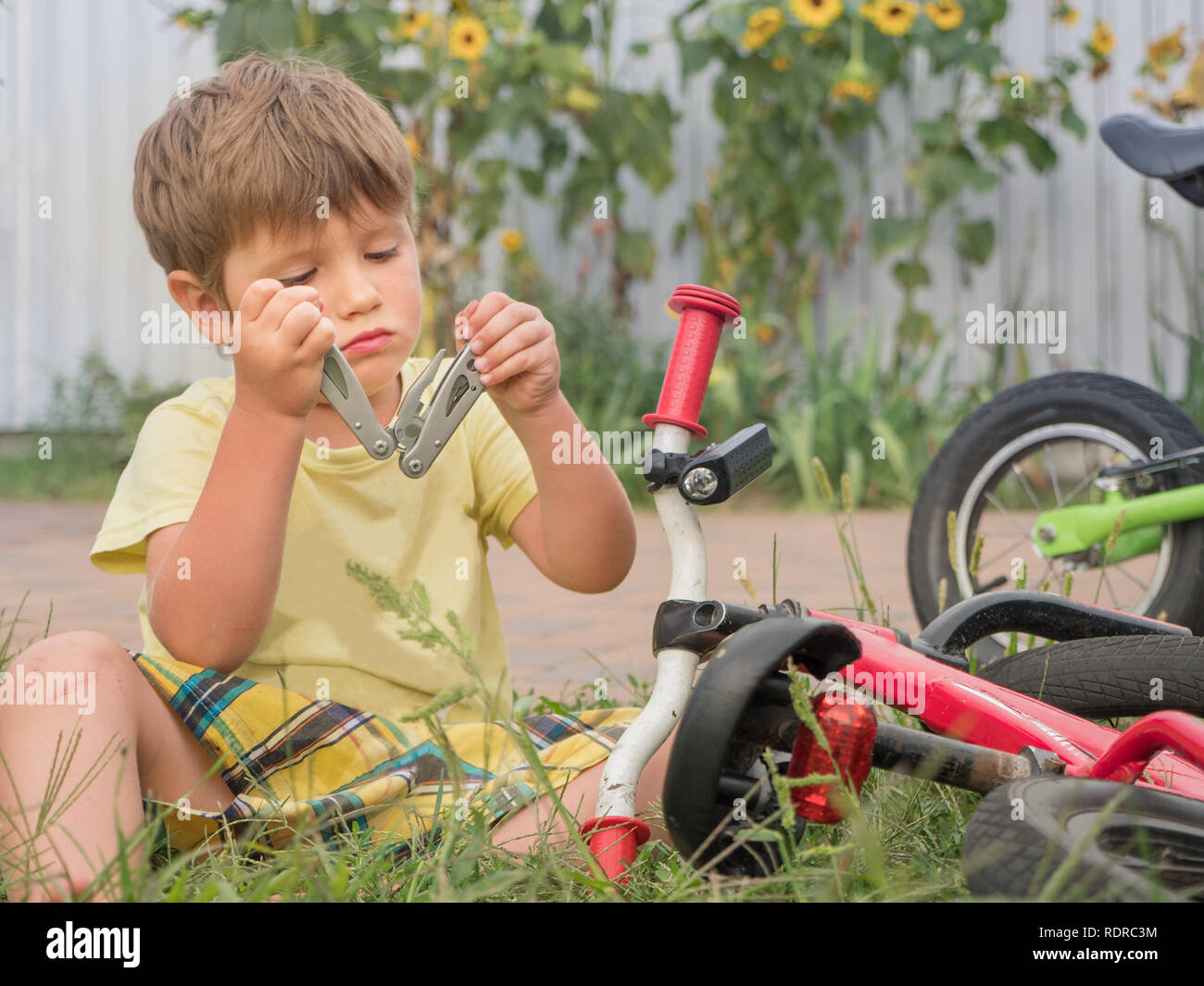 Kid opening multi tool while sitting near the bike. Boy fixing bicycle ...