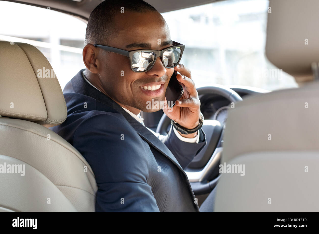 Young businessman driver in sunglasses sitting inside car talking on ...