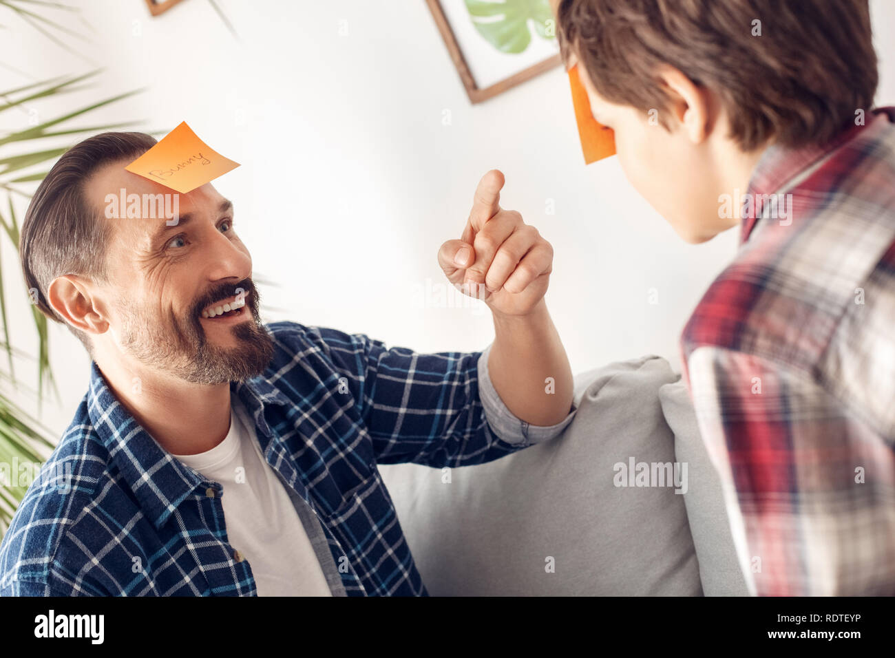 Father and little son at home sitting on sofa playing forehead ...
