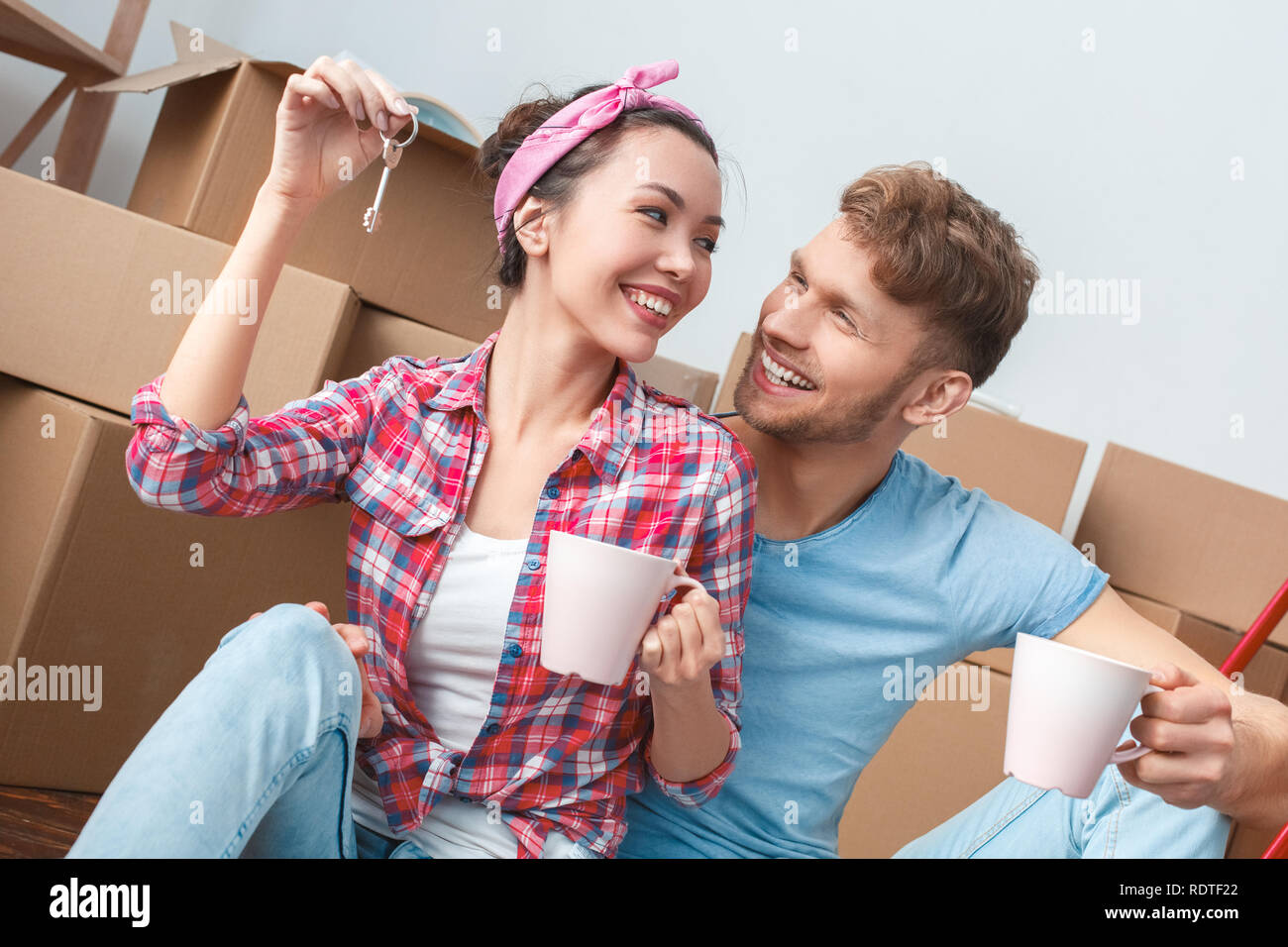 Young couple moving to new place sitting drinking coffee holding keys ...