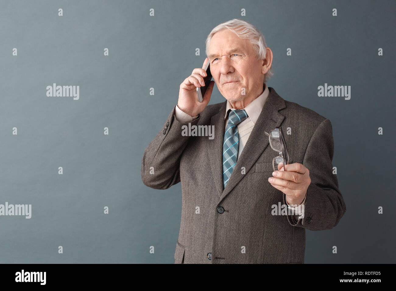 Senior man studio standing isolated on gray holding glasses answering ...