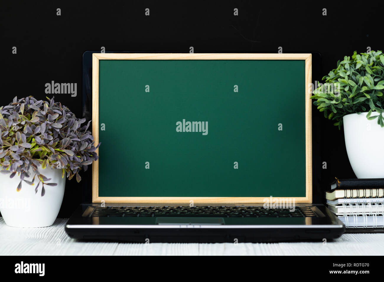 Notebook laptop computer with green chalkboard screen and pile of ...