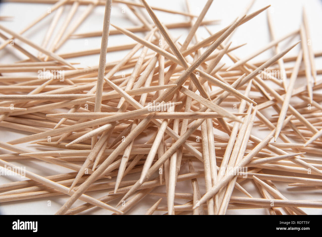 A bunch of unused round wooden toothpicks artfully scattered on a plain ...