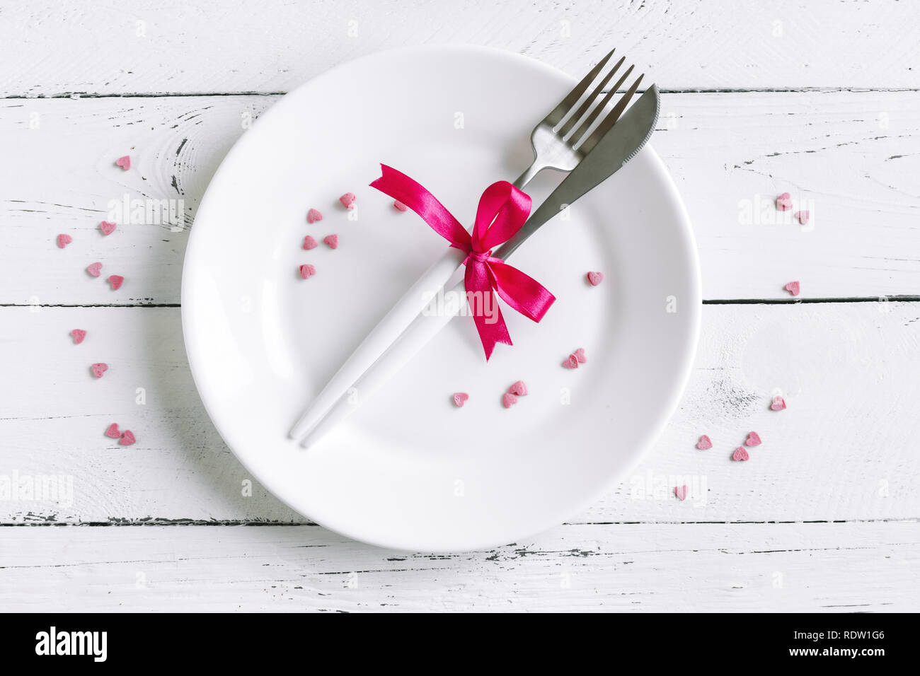 Romantic table setting with white plate, modern cutlery and red ribbon ...