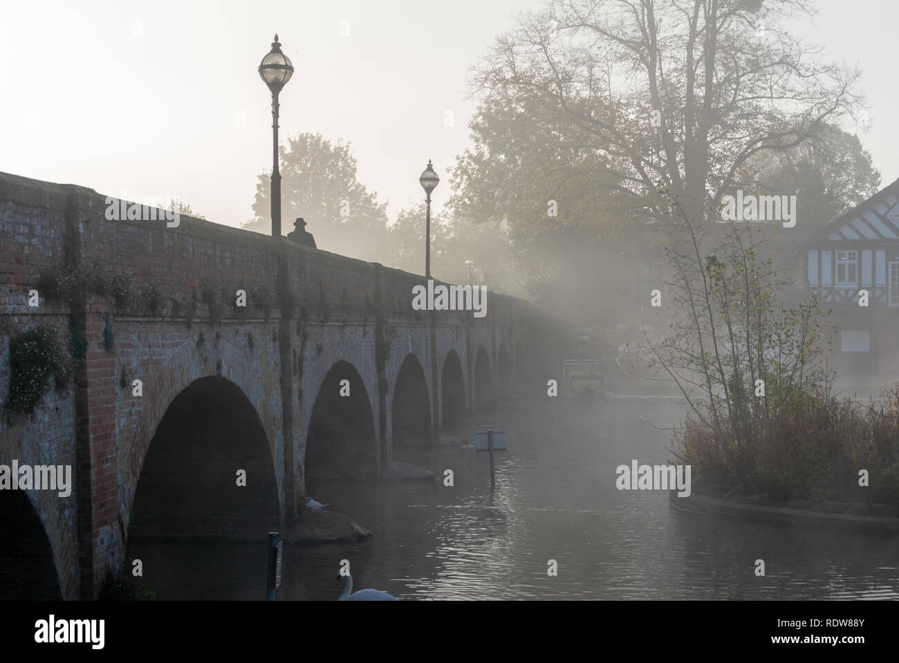 creepy looking man in trilby hat walks across misty arched bridge in ...