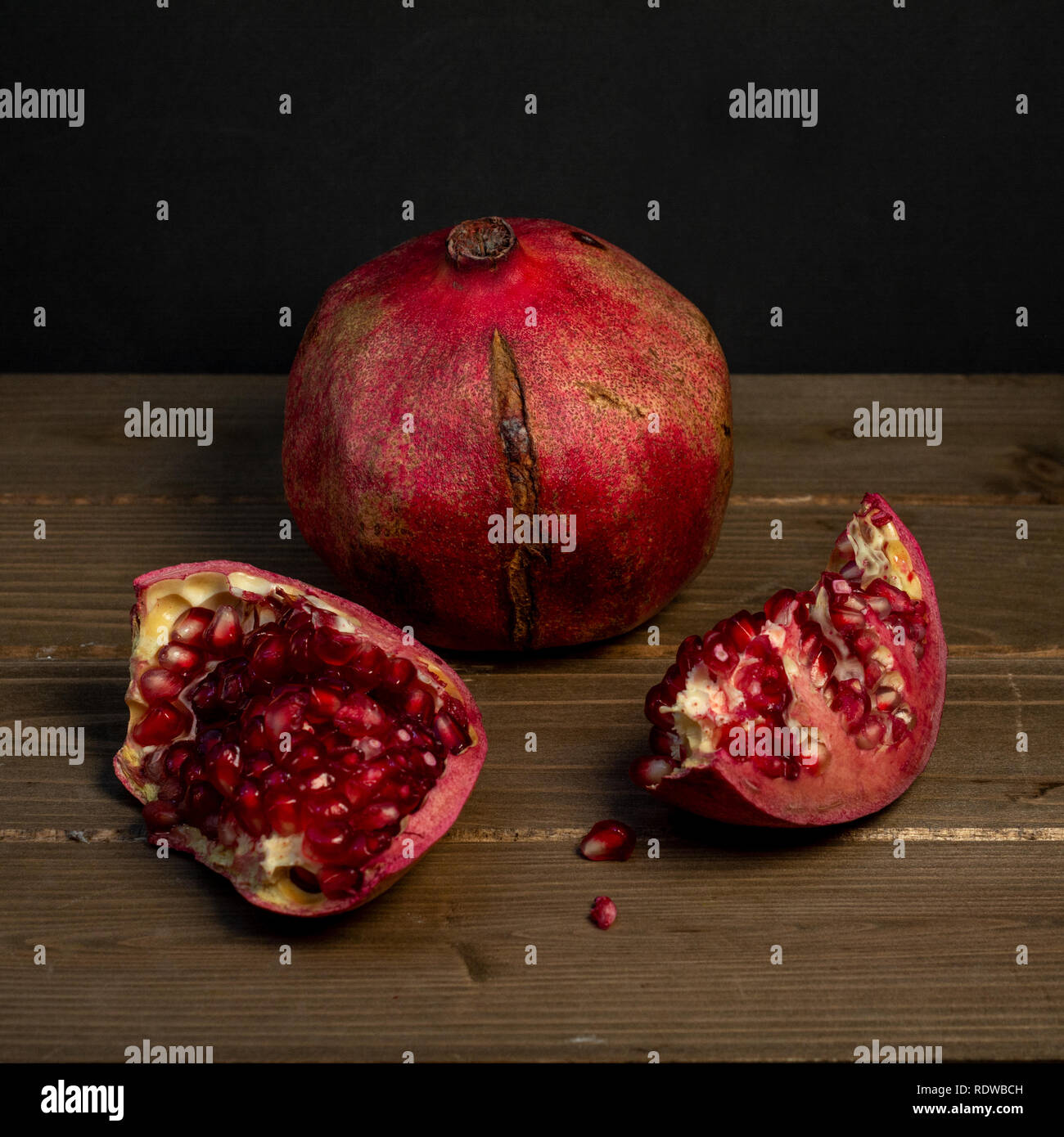 Two pomegranate fruits, one whole and one open, against wooden table ...