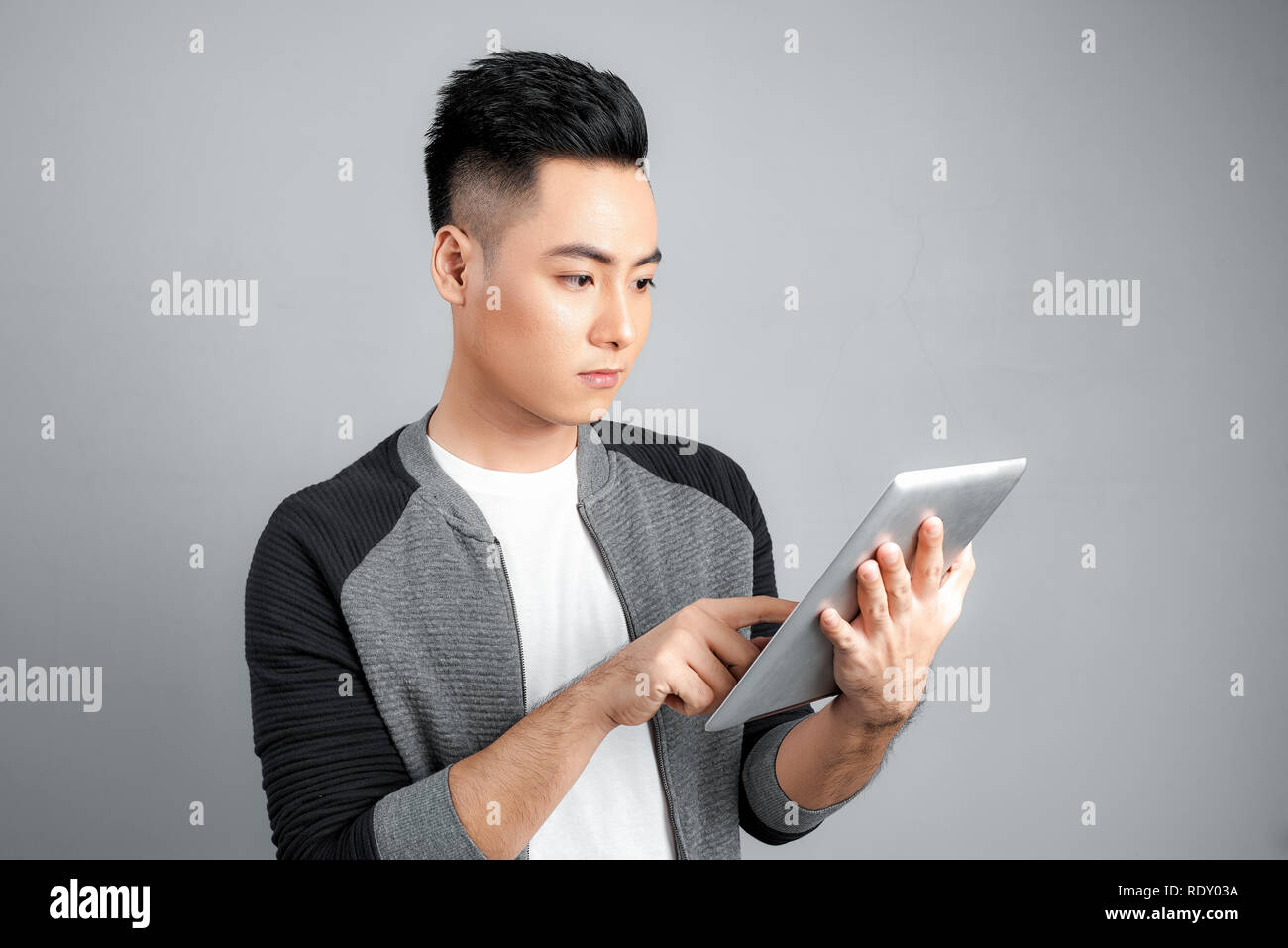 Happy attractive young man standing and using tablet over grey ...