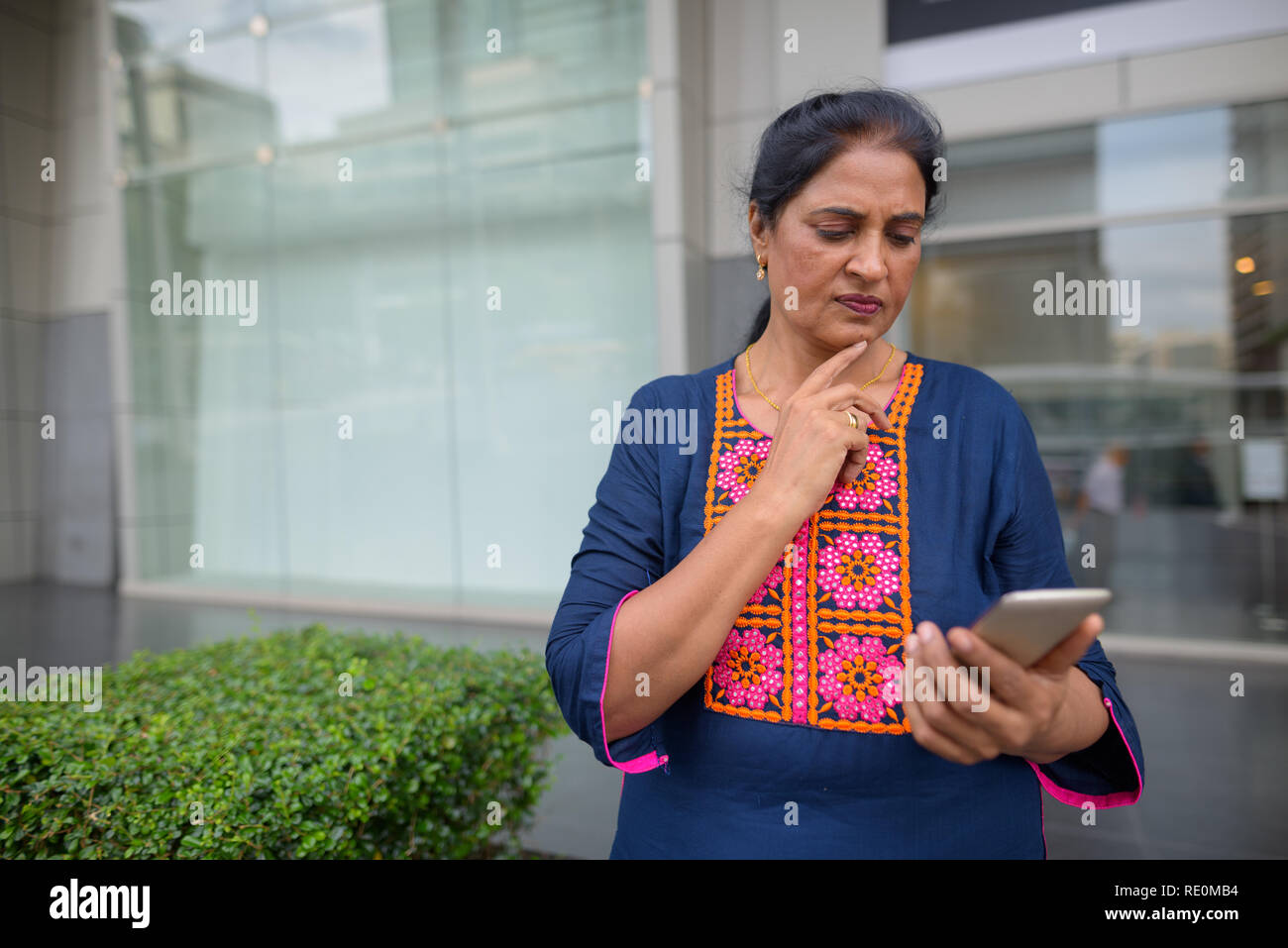 Indian woman using mobile phone in city while thinking Stock Photo - Alamy
