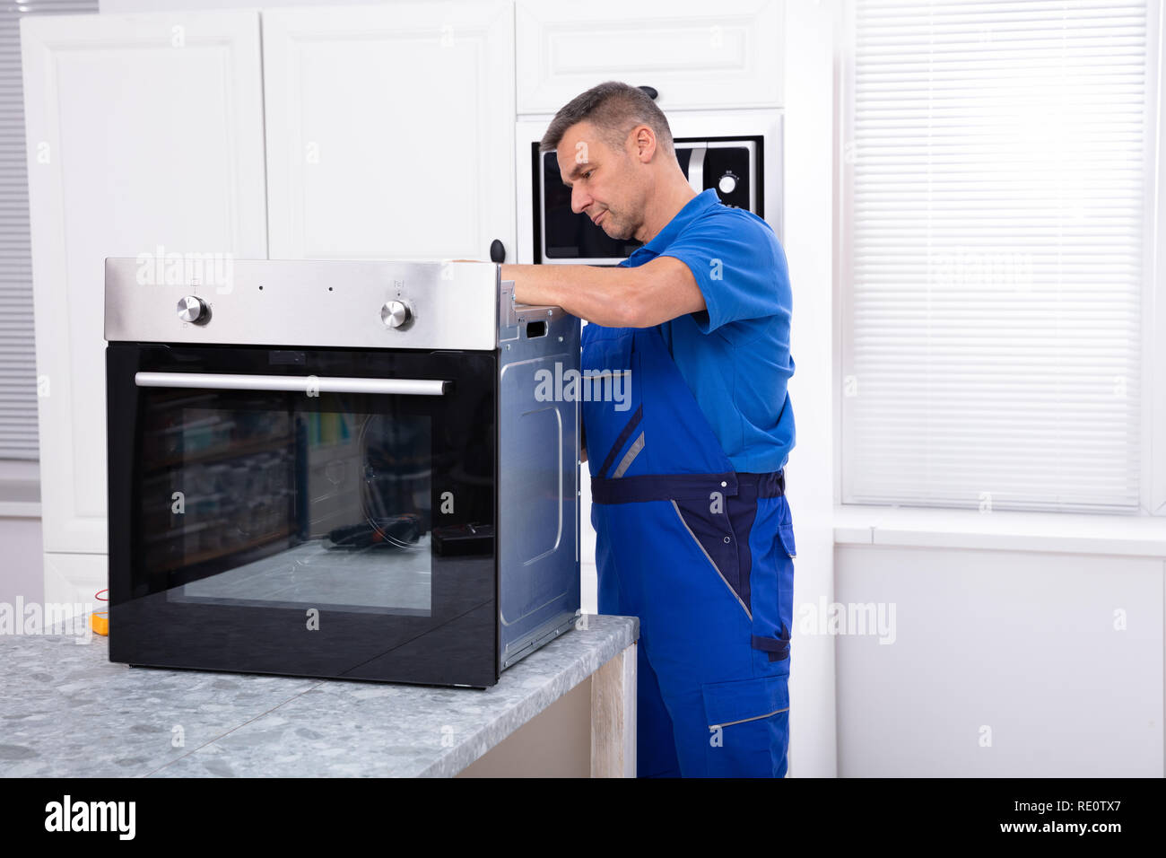 Mature Male Technician Repairing Oven On Kitchen Worktop Stock Photo ...