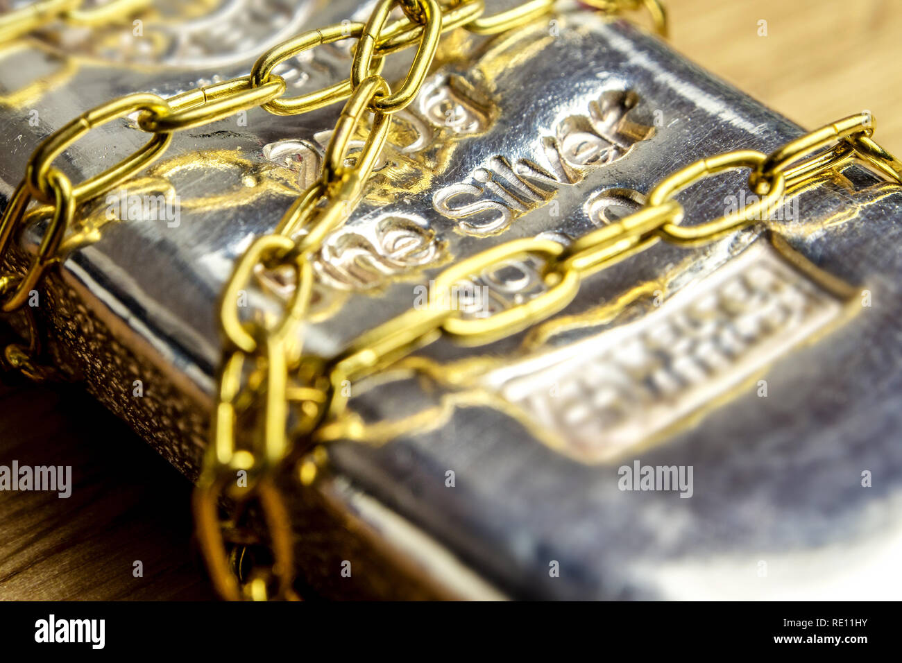 closeup of silver brick in golden chains laying on wooden background ...