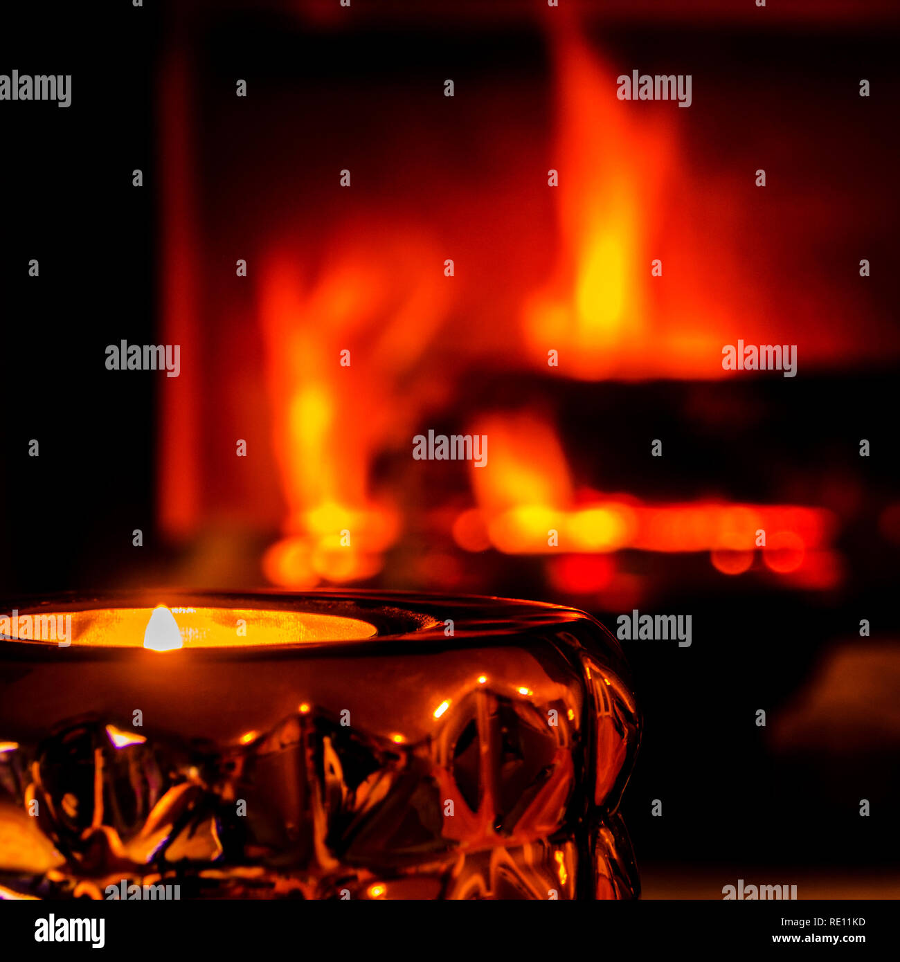 closeup of lit candle with blurred fireplace fired up in the background ...