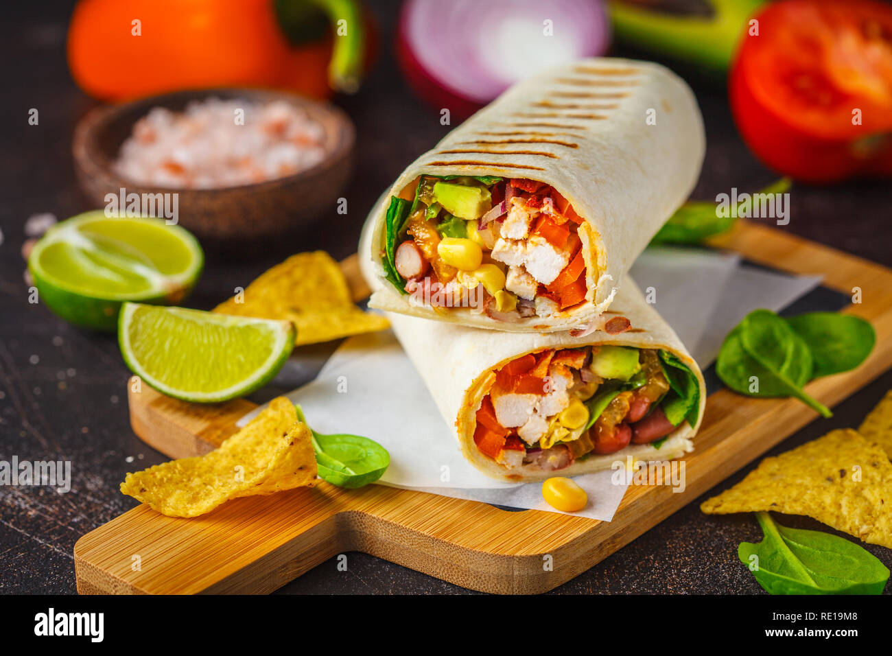 Grilled burritos wraps with chicken, beans, corn, tomatoes and avocado on a wooden board, dark ...