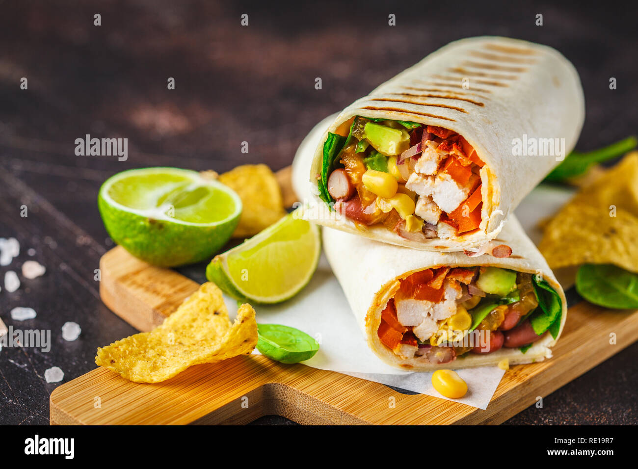 Grilled burritos wraps with chicken, beans, corn, tomatoes and avocado on a wooden board, dark ...