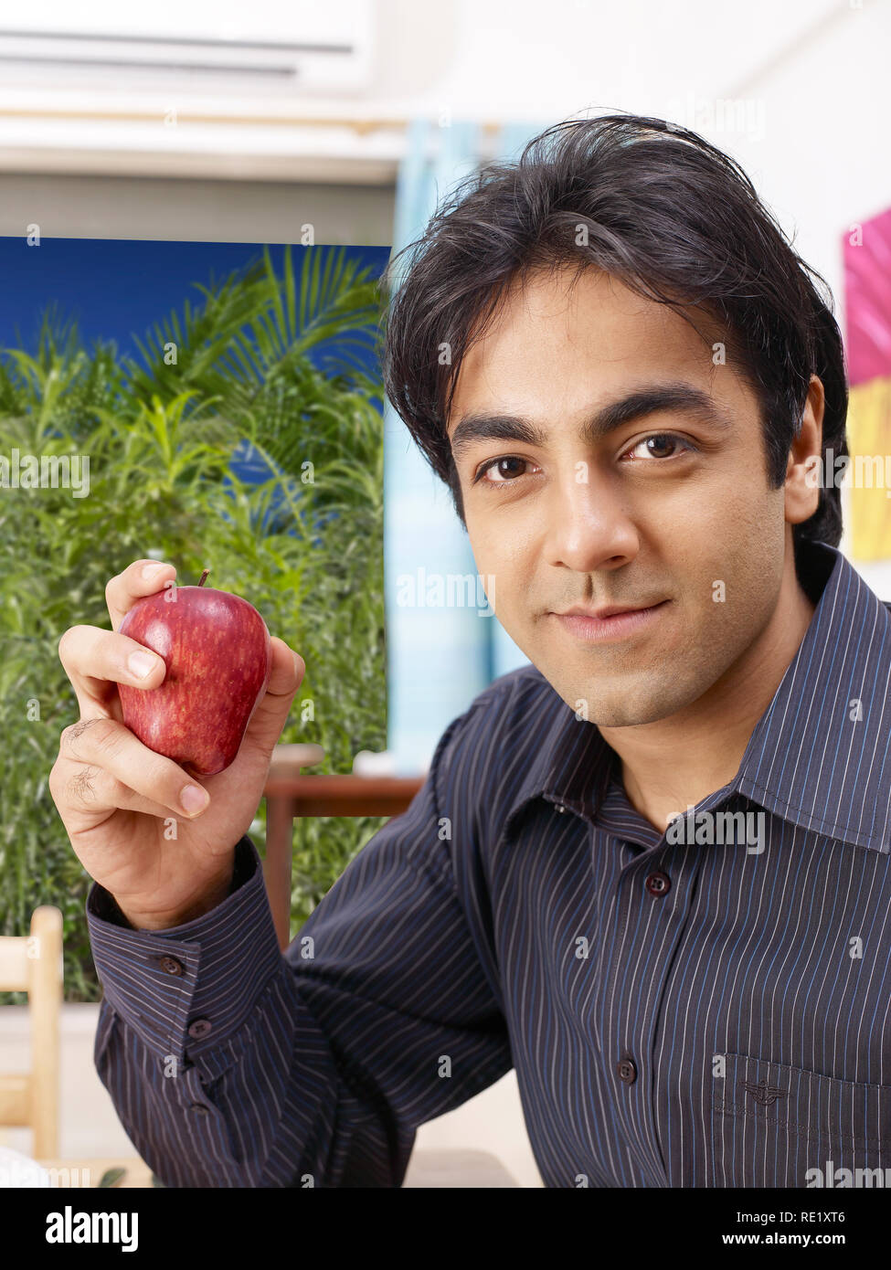YOUNG MAN HOLDING AN APPLE SITTING ON A TABLE IN HIS HOME Stock Photo ...