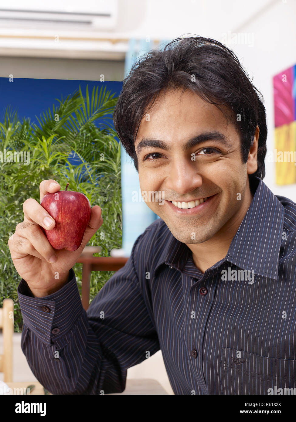 YOUNG MAN HOLDING AN APPLE SITTING ON A TABLE IN HIS HOME Stock Photo ...