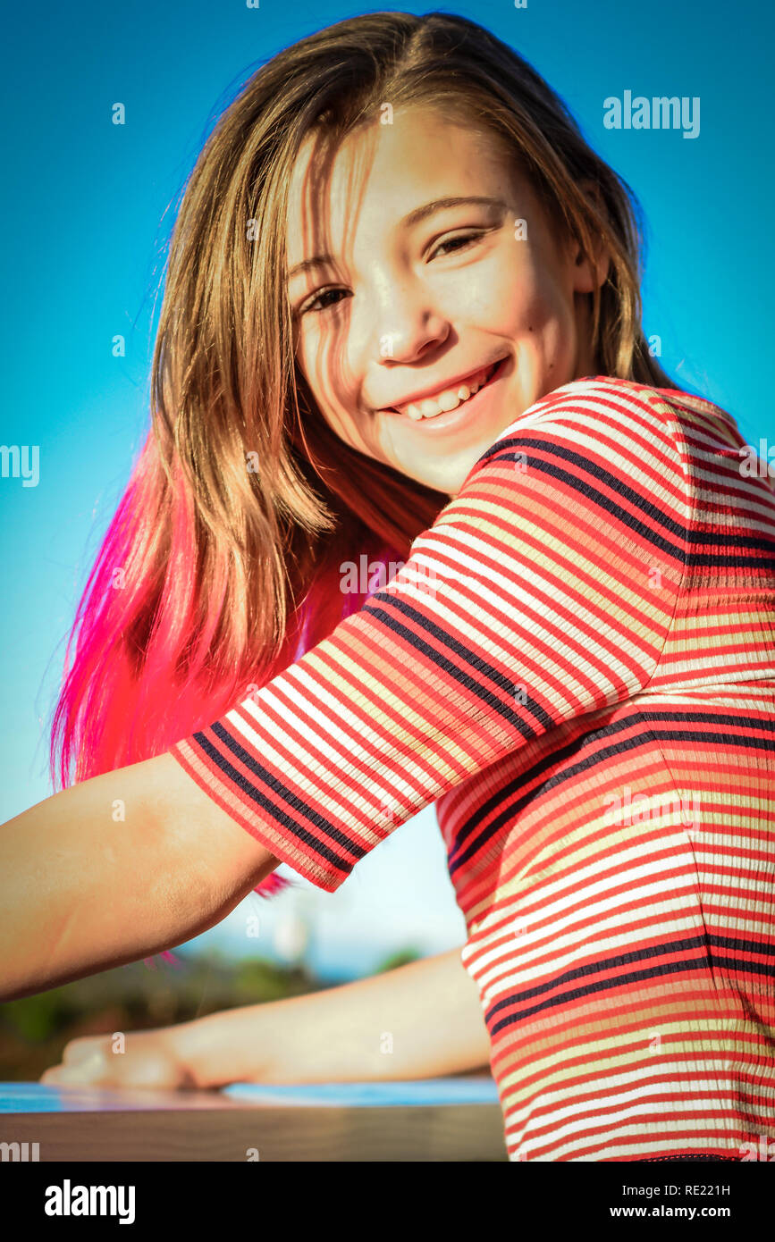 Happy tween with trendy pink hair smiles while bracing herself on ...