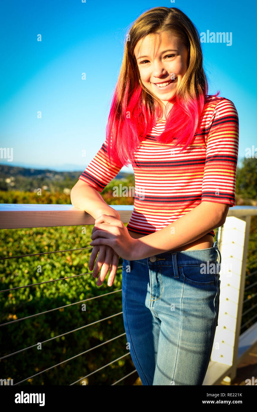 Happy tween with trendy pink hair, smiles while leaning on balcony rail ...