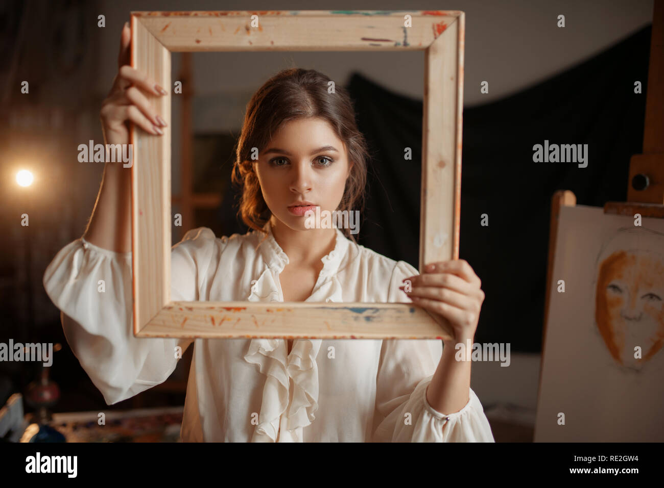 Female painter holds wooden frame at her face in studio, portrait ...