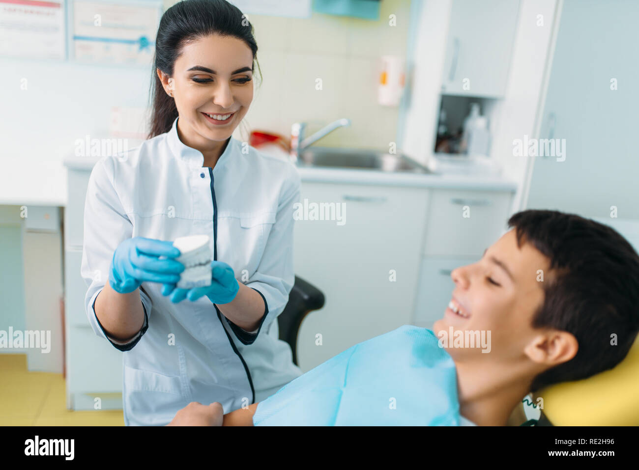 Female dentist shows dentures to little boy in a dental chair ...