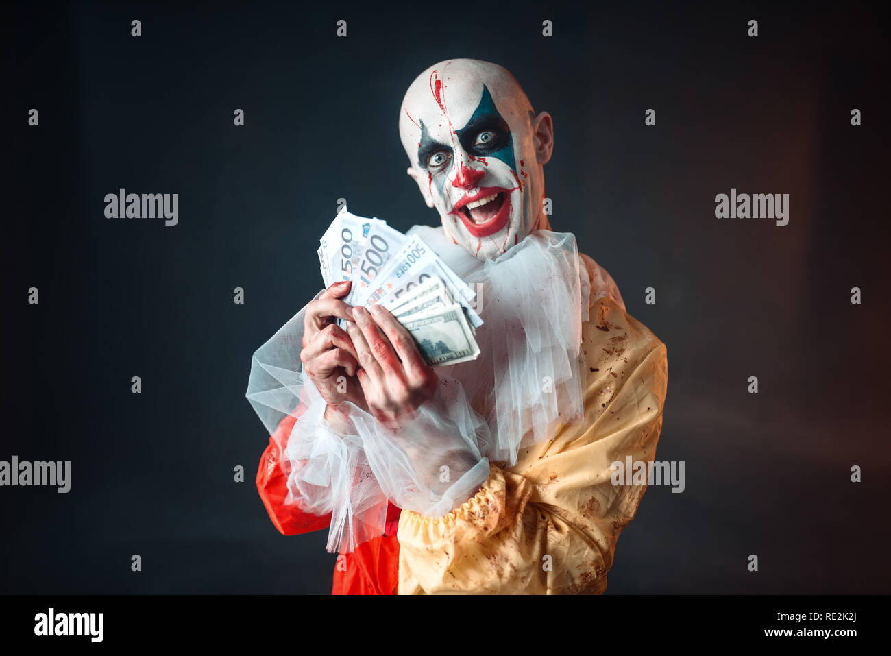 Scary bloody clown with crazy eyes holds fan of money. Man with makeup ...
