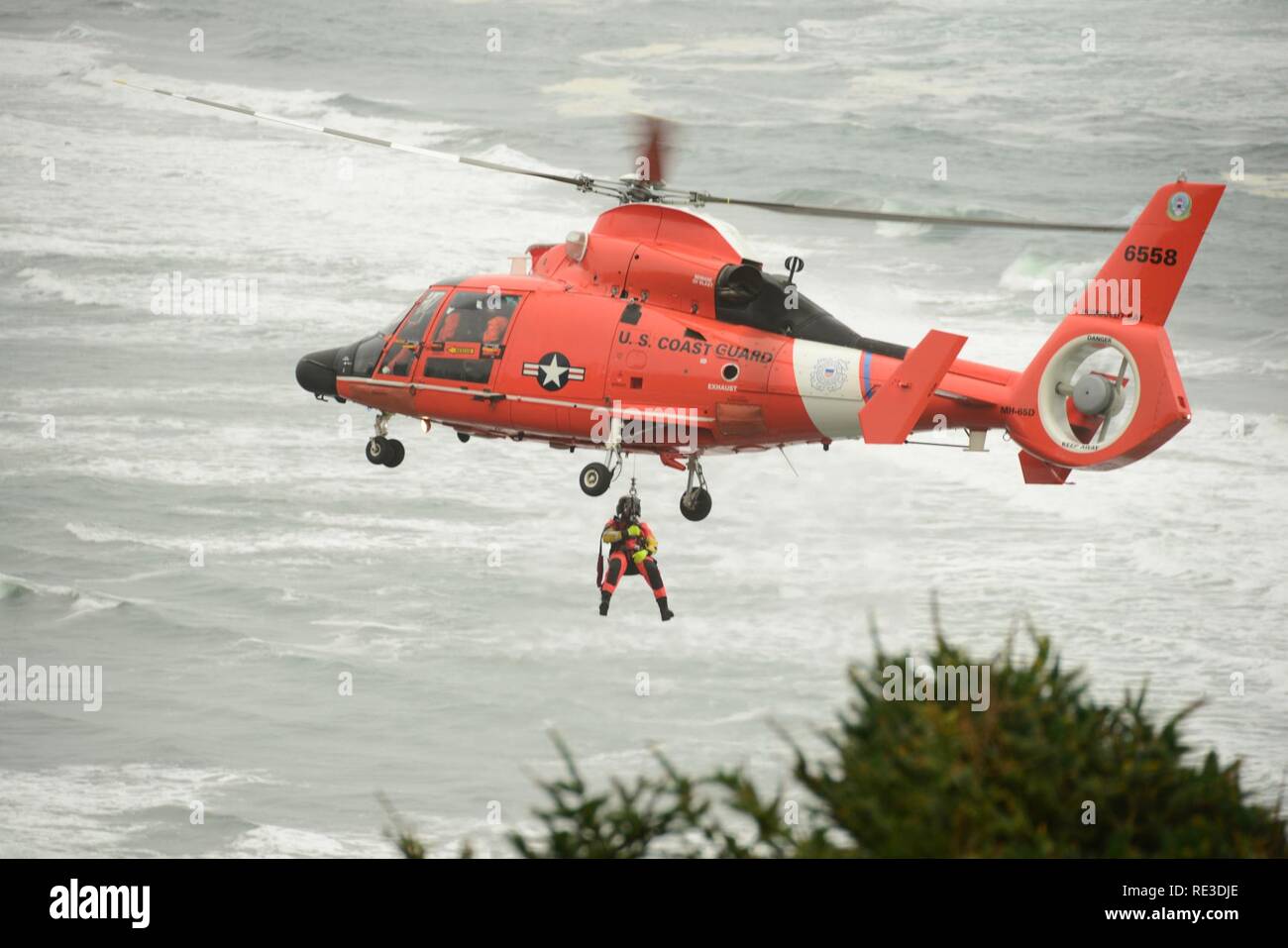 An aviation survival technician is lowered from an MH-65 Dolphin ...