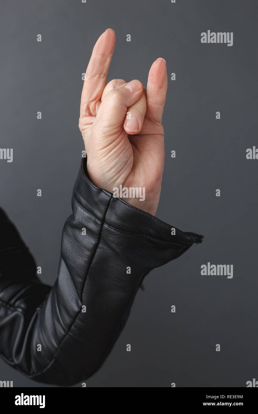 Senior man in leather jacket standing isolated on gray showing horns ...