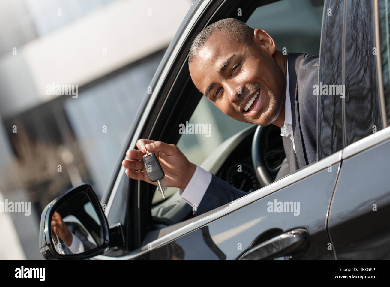 Young man sitting in new car looking out from window with key looking ...