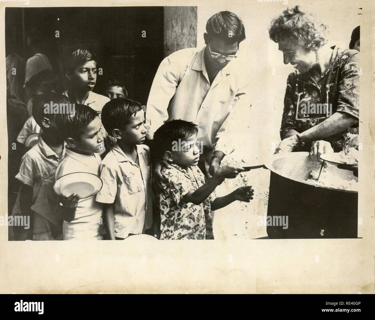 CHILDREN IN LINE FOR FOOD. ONE MAN DIRECTING THE CHILDREN, AND ONE MAN ...