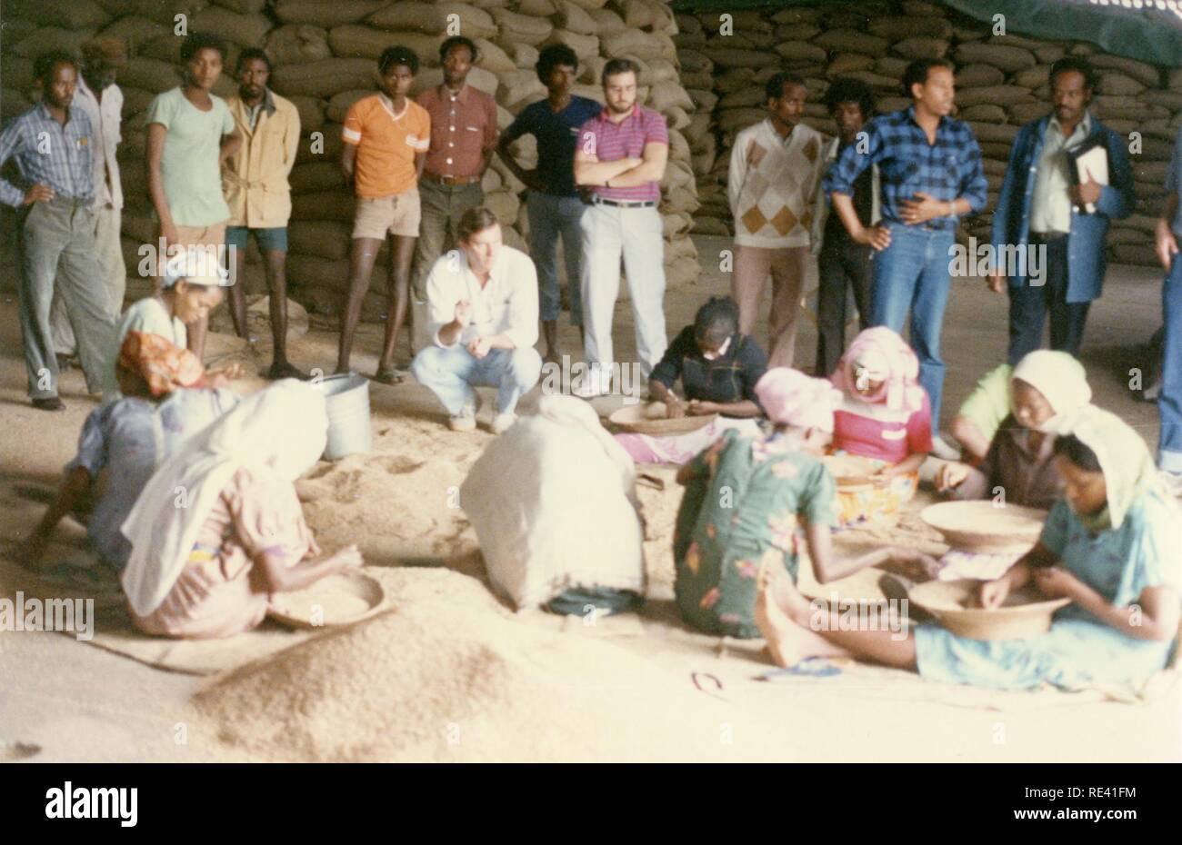 MEN STANDING AROUND OBSERVING WOMEN GRATING SAND BY HAND Stock Photo ...