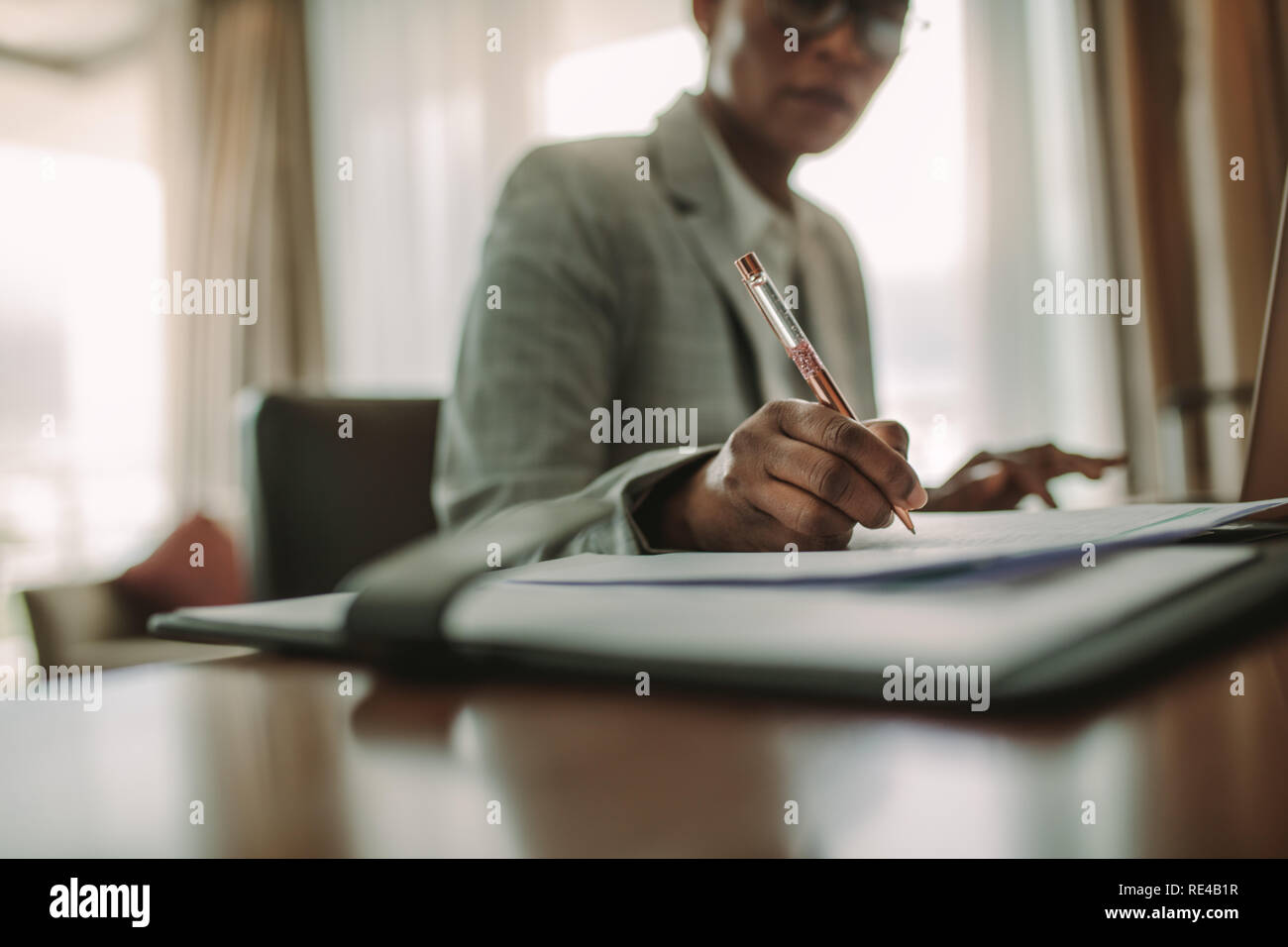Businesswoman sitting at hotel room desk writing on document. Focus on ...