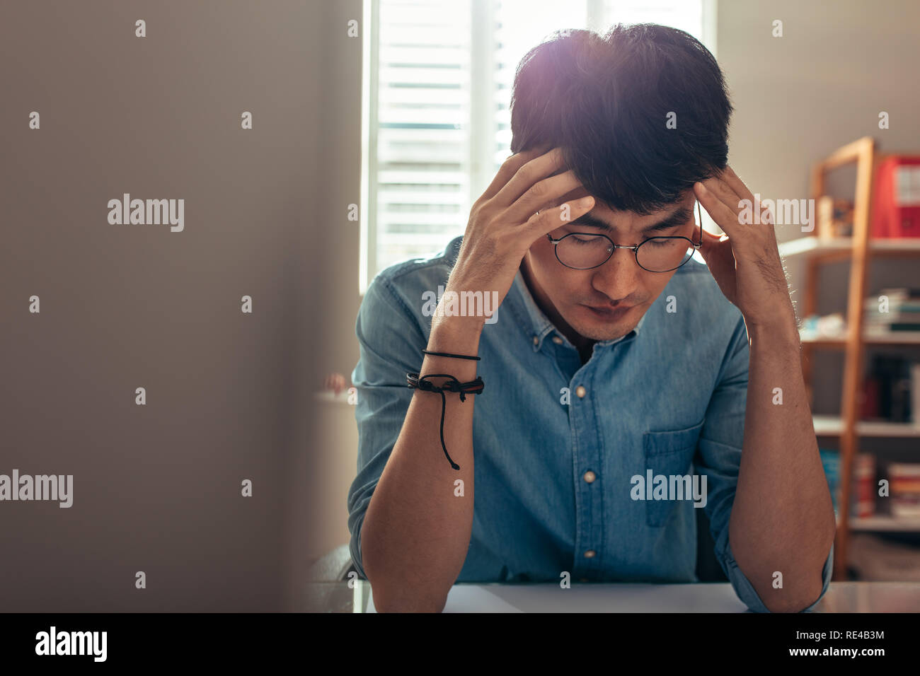 Man sitting at his desk looking stressed and tired. Man holding head in ...